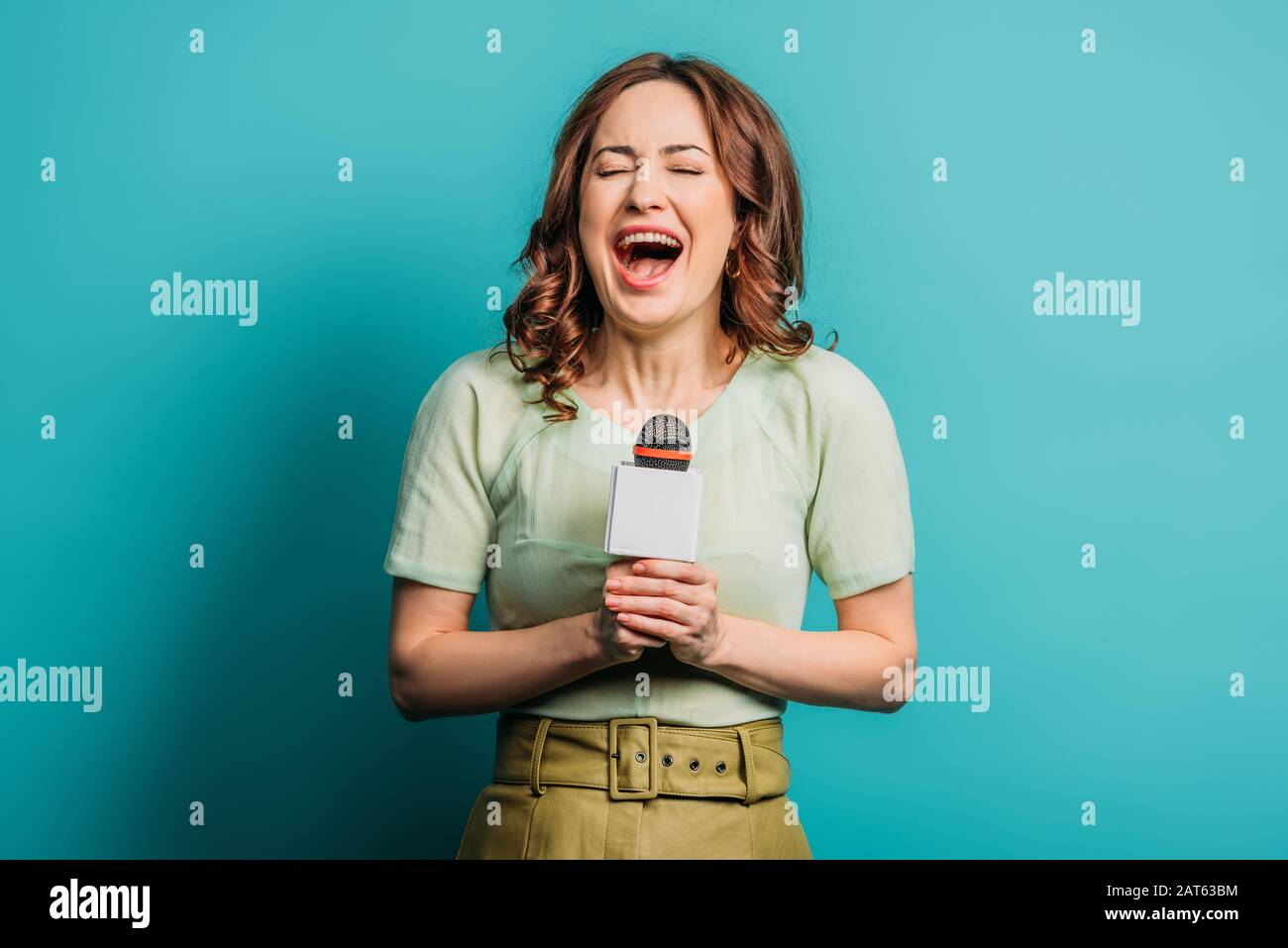 cheerful journalist laughing while holding microphone on blue ...