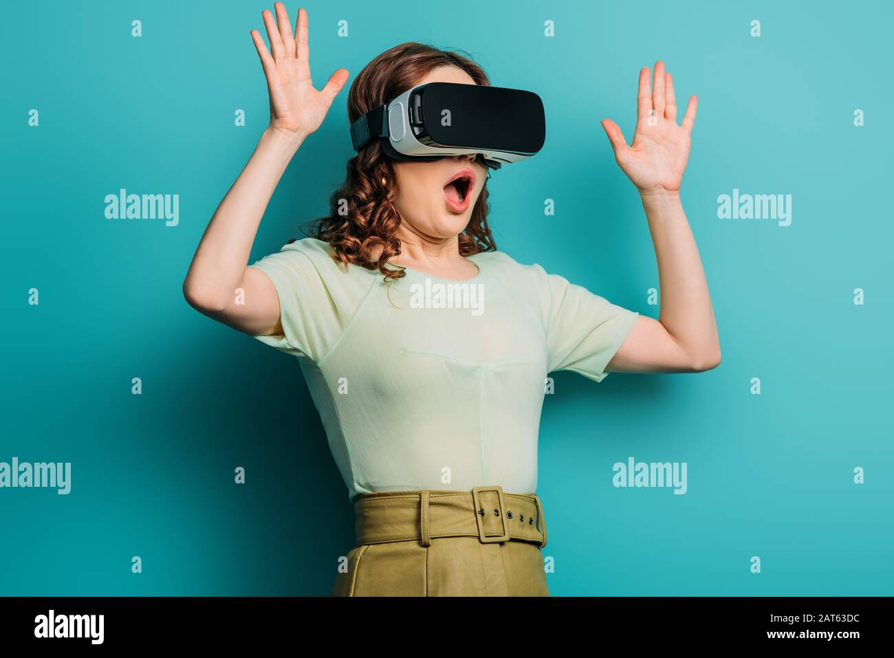scared girl in vr headset standing with raised hands on blue background ...