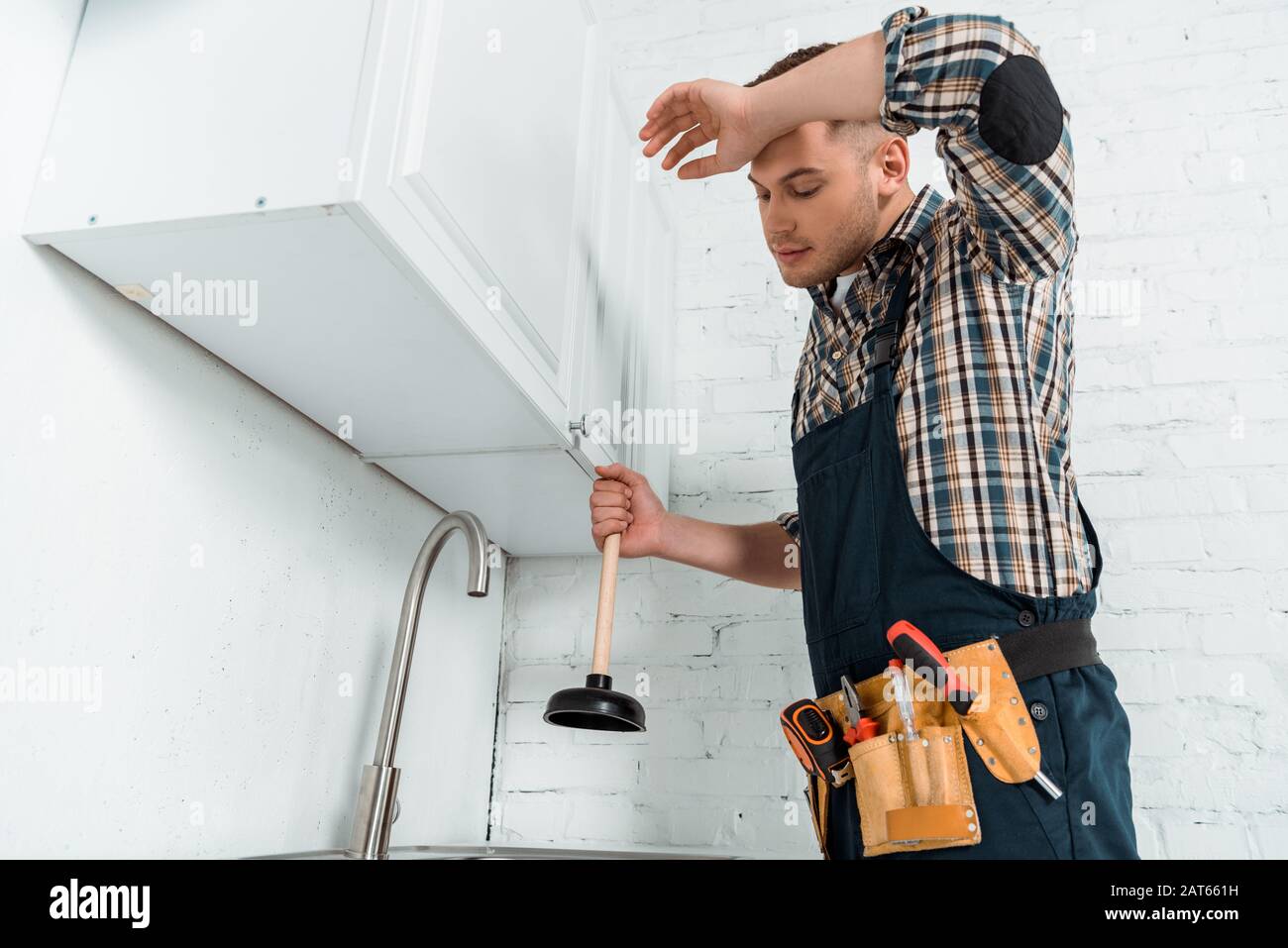 tired installer holding plunger near faucet in kitchen Stock Photo - Alamy