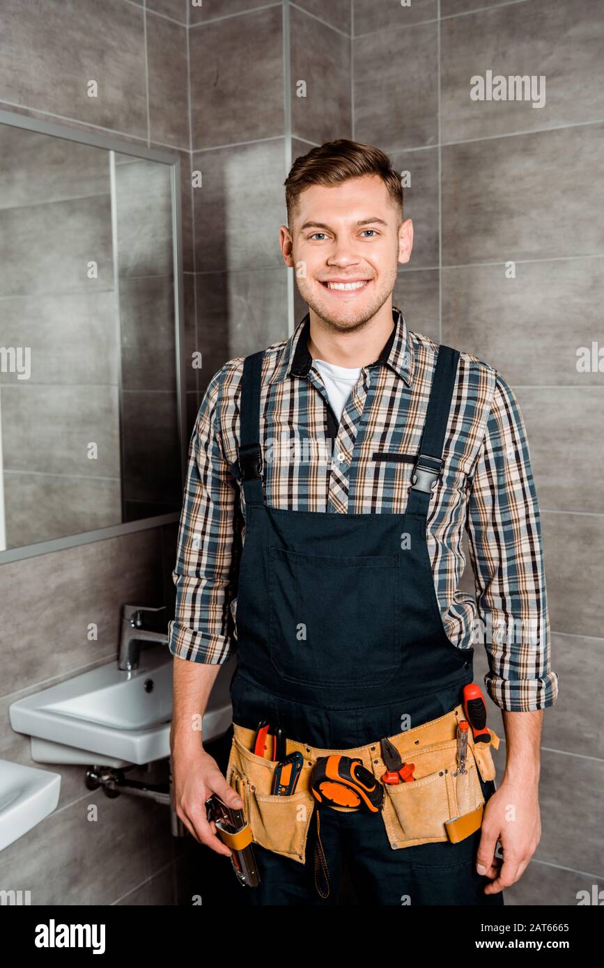 happy installer with tool belt standing in bathroom Stock Photo - Alamy