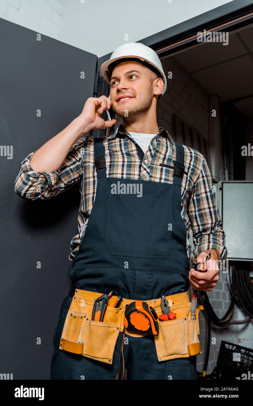 happy installer in safety helmet holding screwdriver while talking on ...