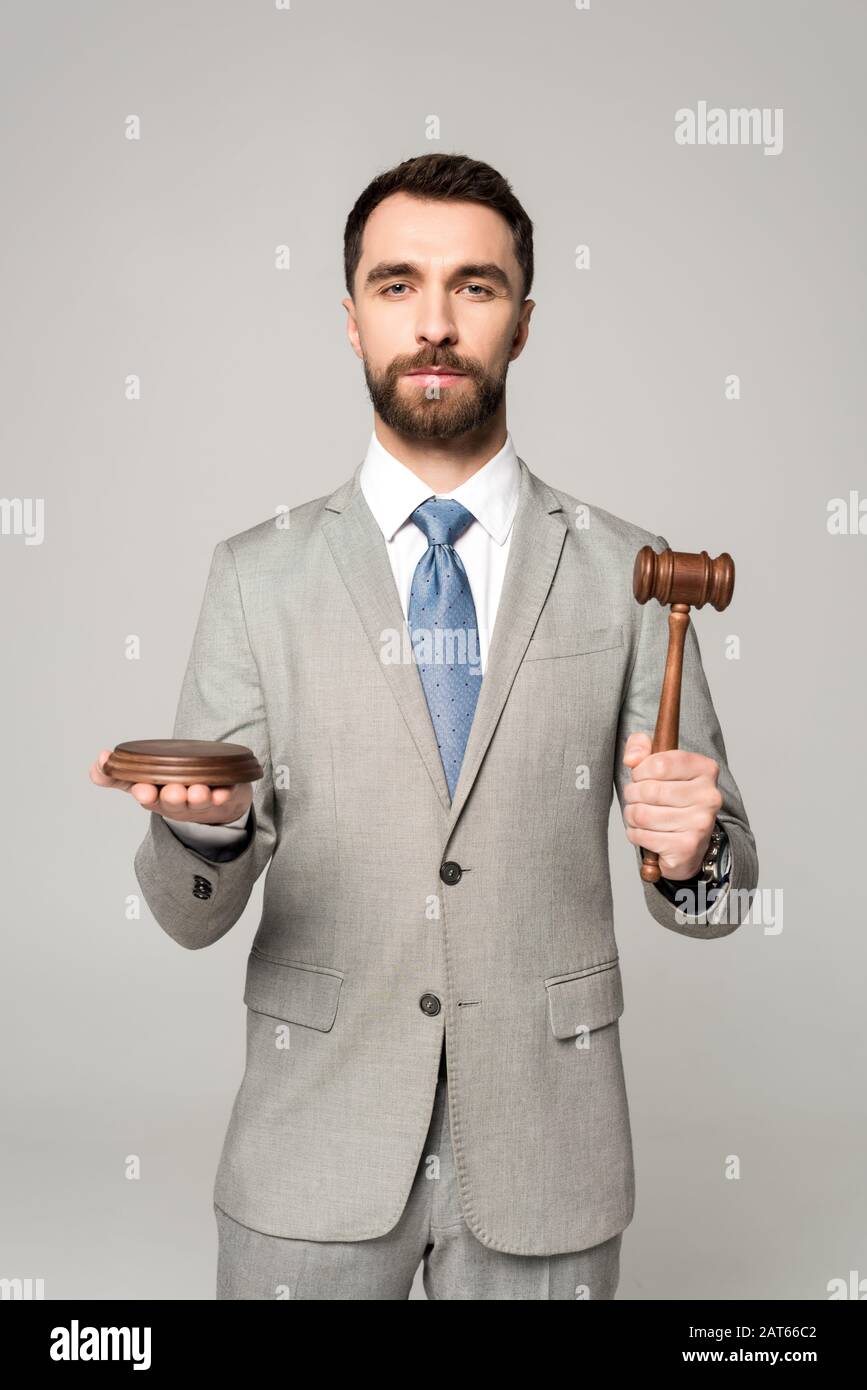 confident judge holding gavel while looking at camera isolated on grey ...