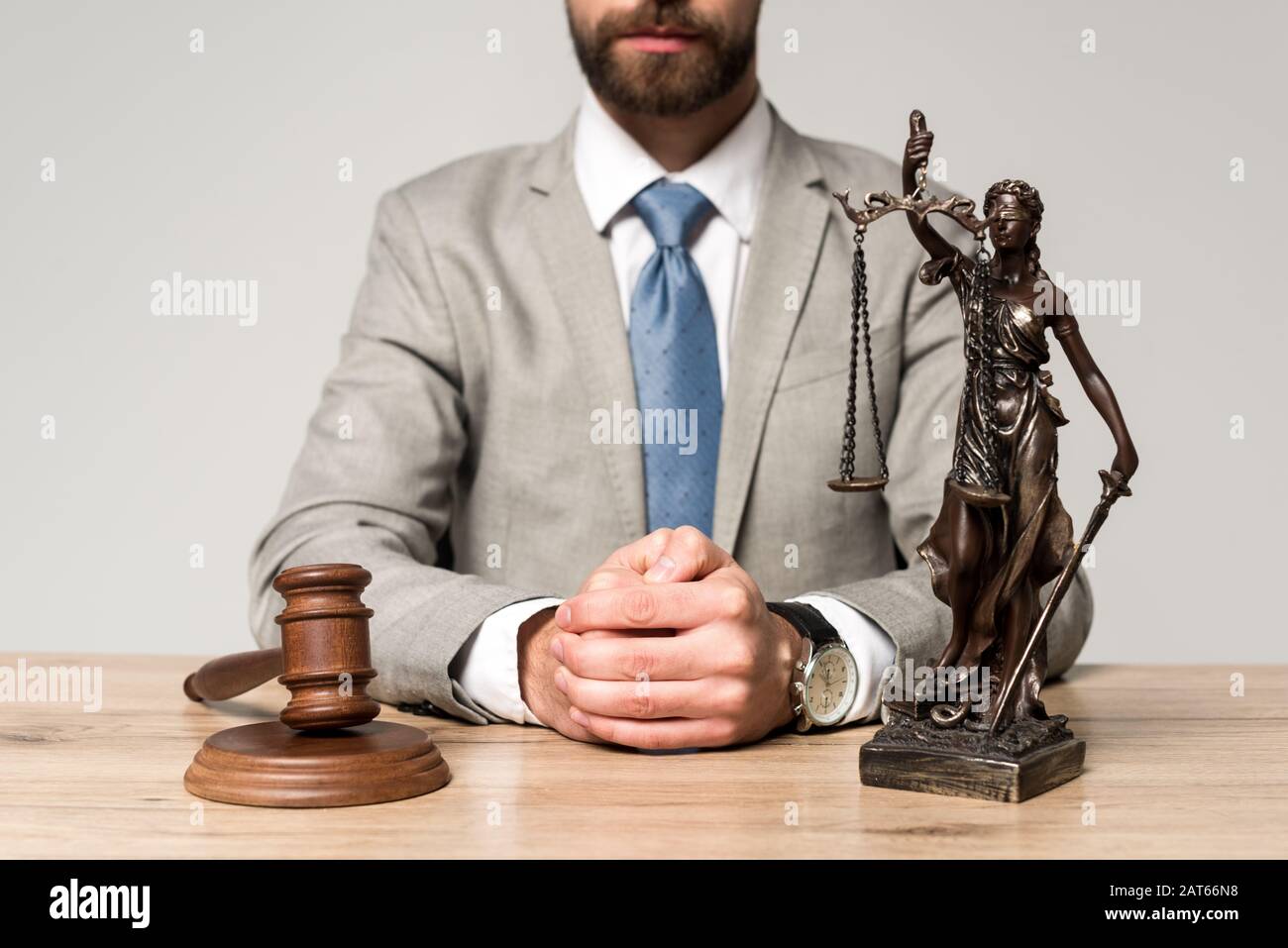 partial view of judge sitting at desk near gavel and themis statue ...