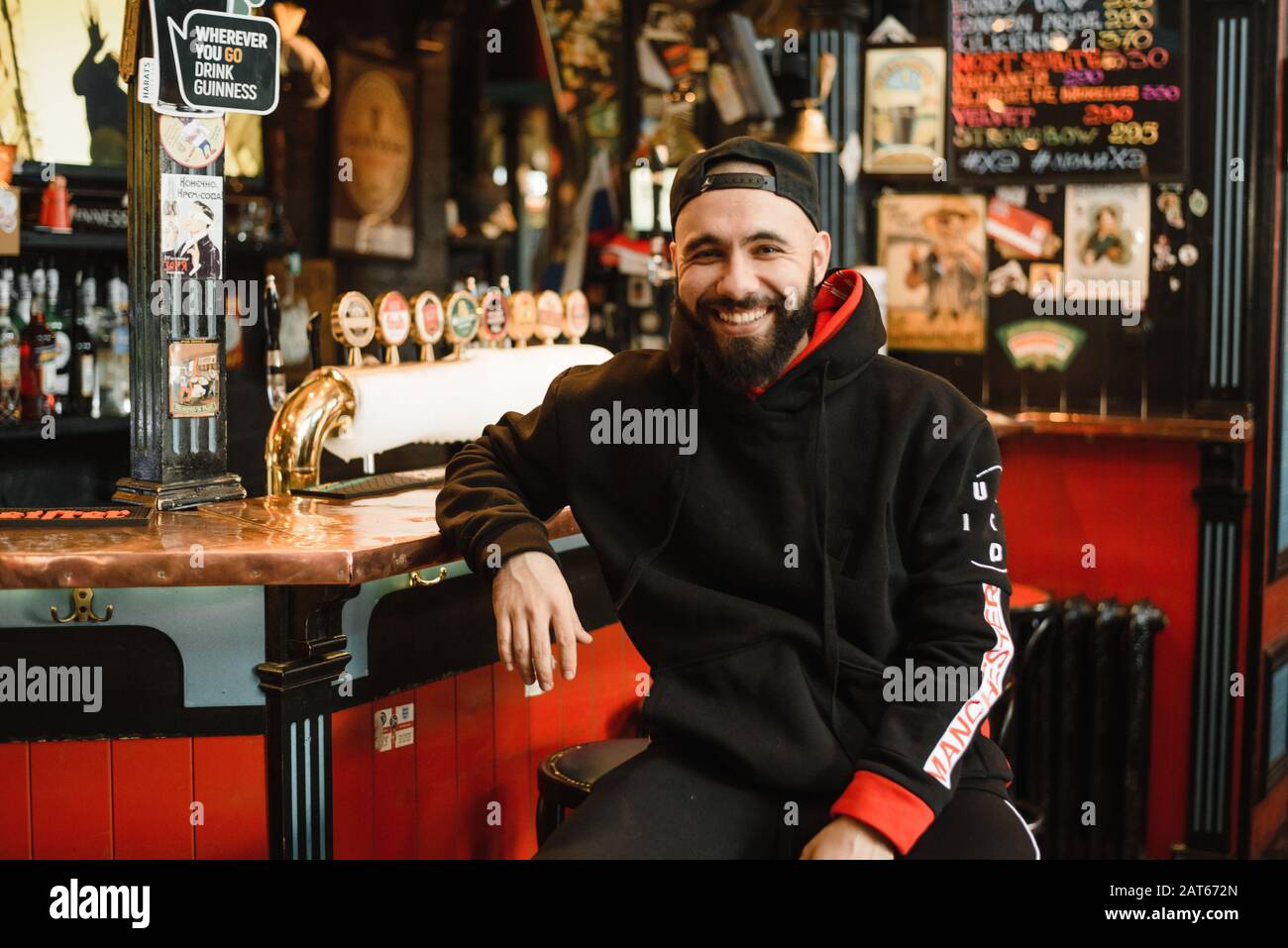 A young man sits in a bar against the bar counter. Looks at the camera ...