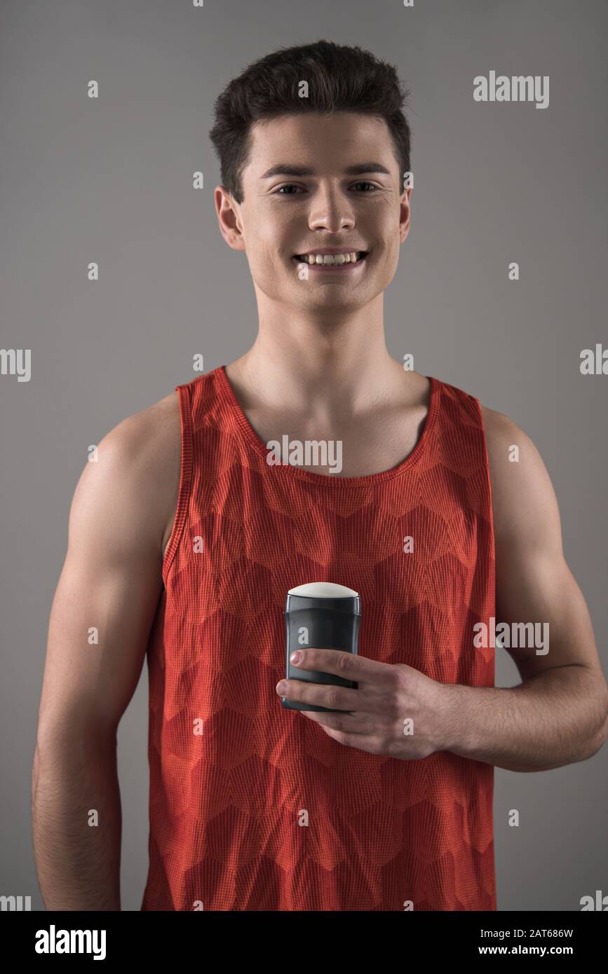 young man in red sleeveless shirt holding deodorant while smiling at ...