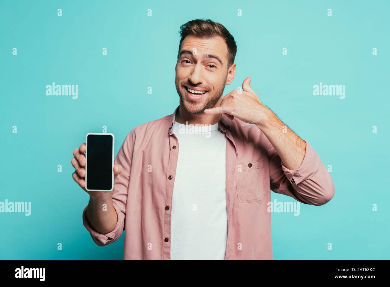 cheerful handsome man showing call me sign smartphone with blank screen ...