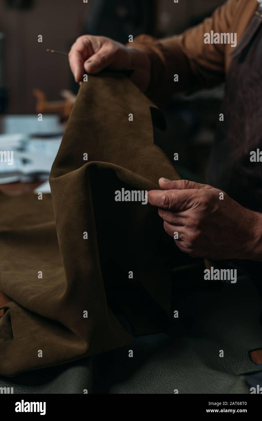cropped view of cobbler holding piece of genuine leather in workshop ...