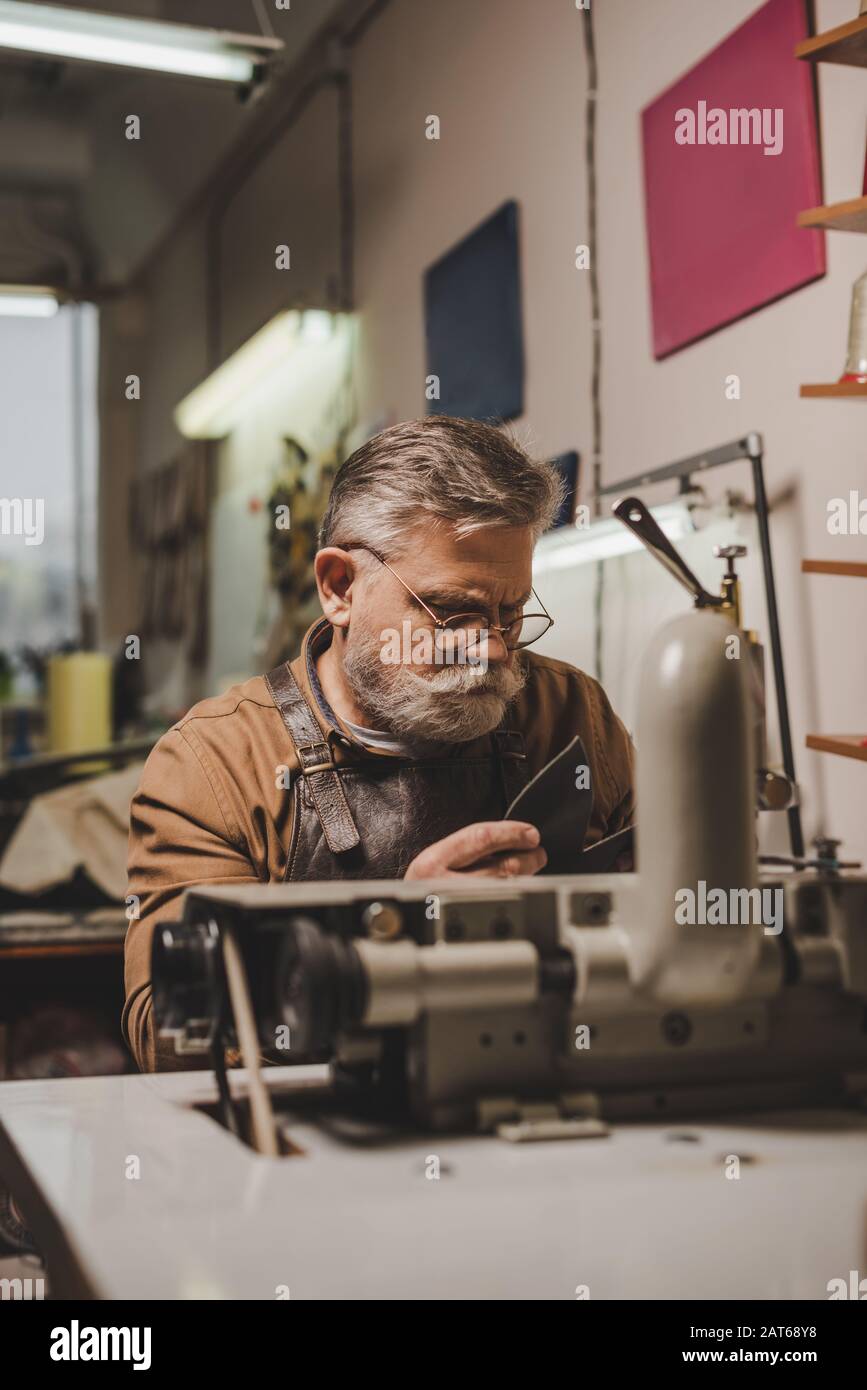 selective focus of senior shoemaker sewing leather on sewing machine in ...