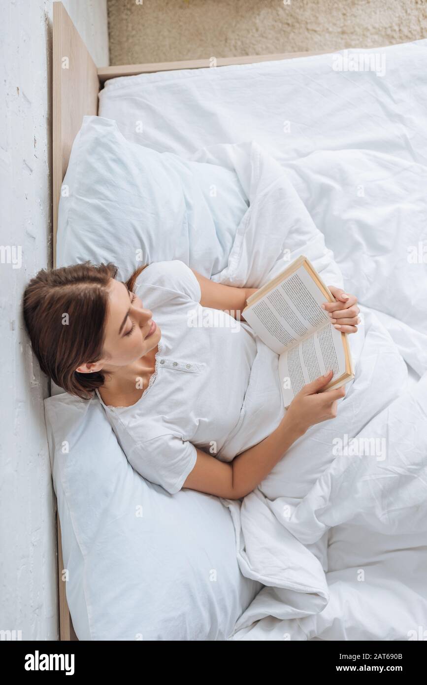 top view of happy girl reading book while chilling in bed Stock Photo ...