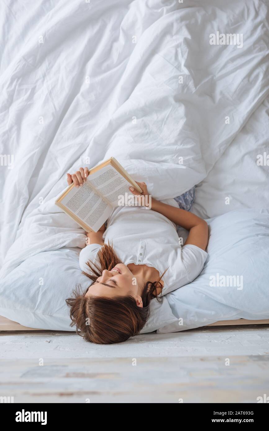 top view of smiling girl reading book while chilling in bed Stock Photo ...
