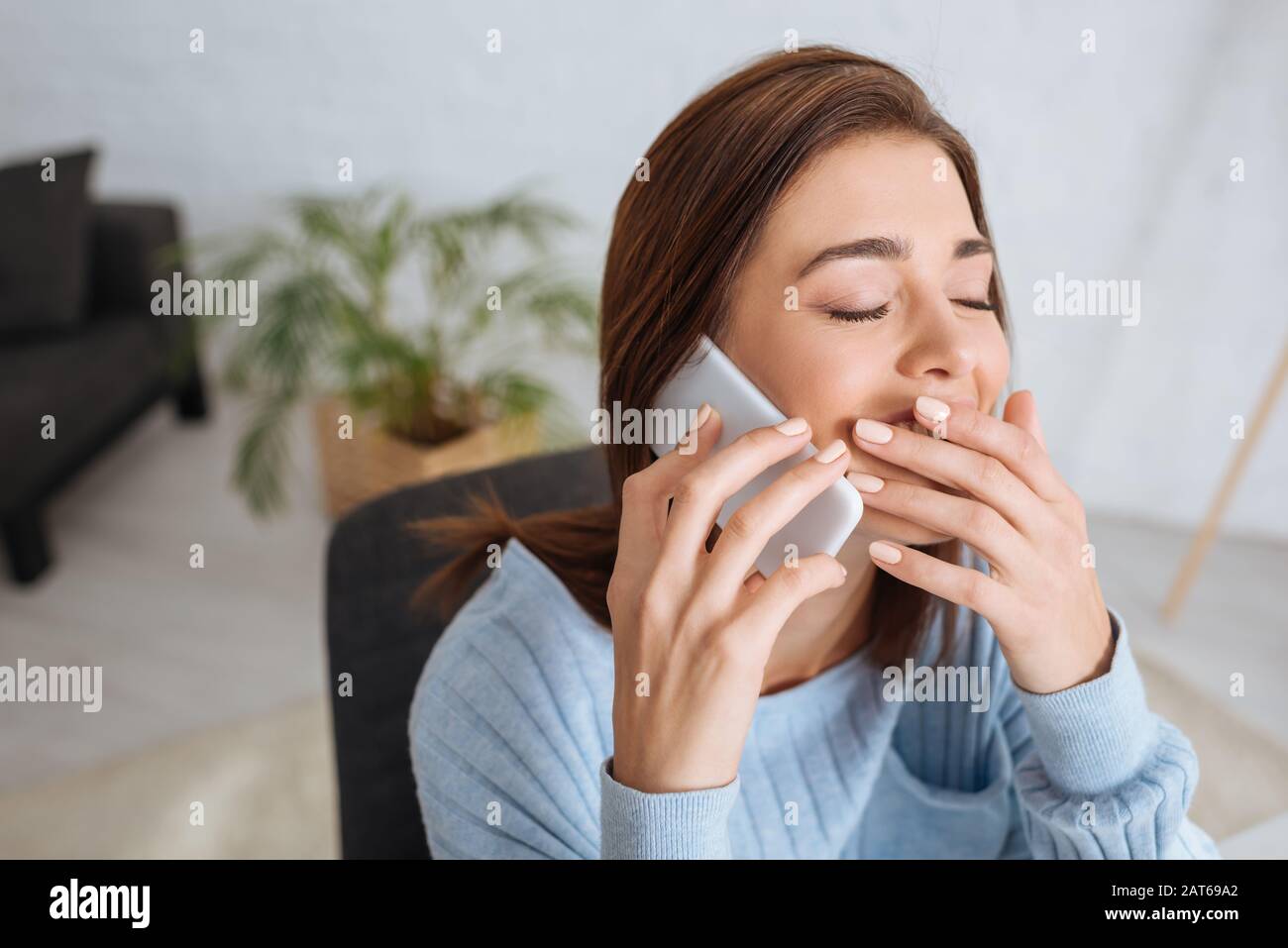 happy young woman laughing while talking on smartphone and covering ...