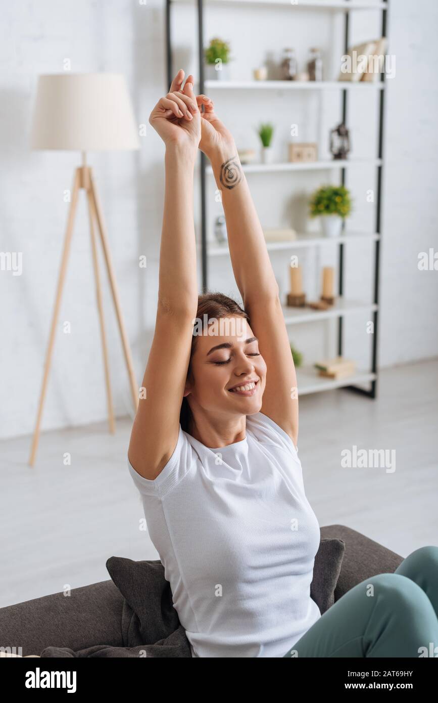 tattooed woman with outstretched hands smiling and relaxing in living ...