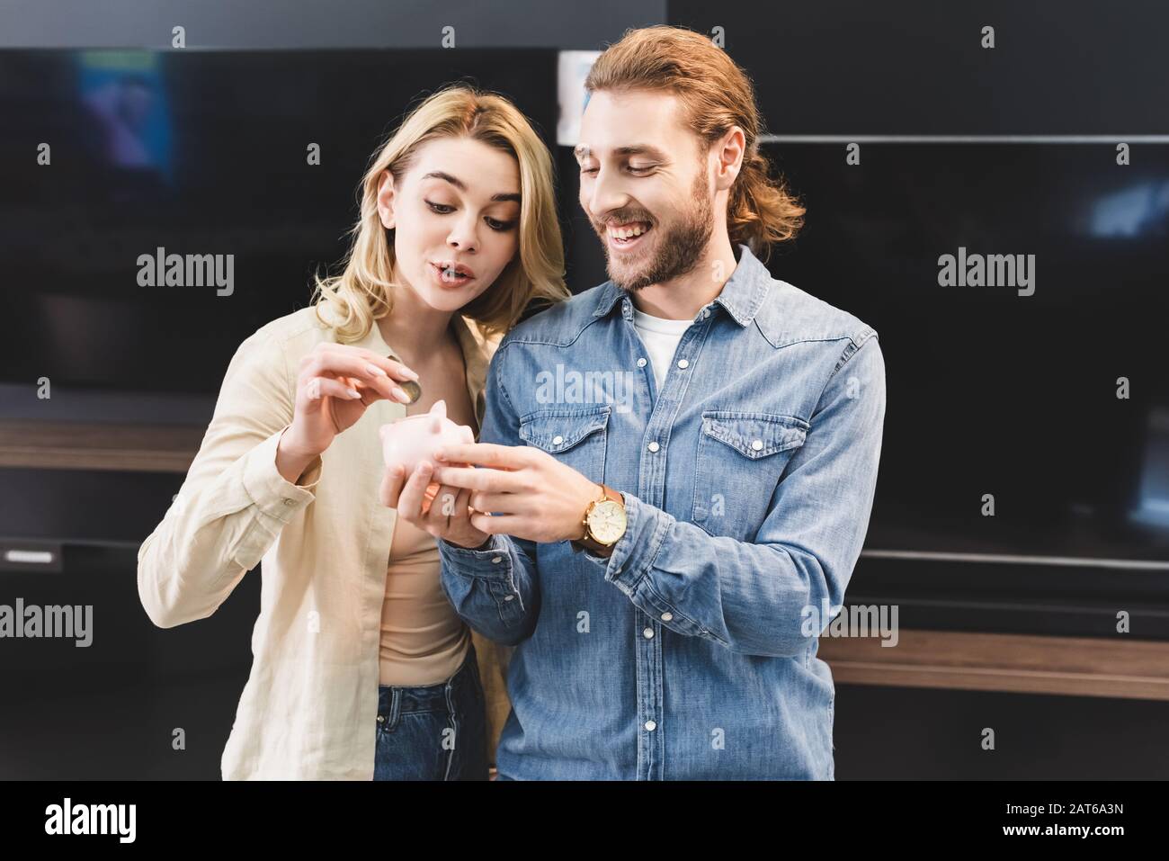 smiling boyfriend holding piggy bank and girlfriend putting coin into ...