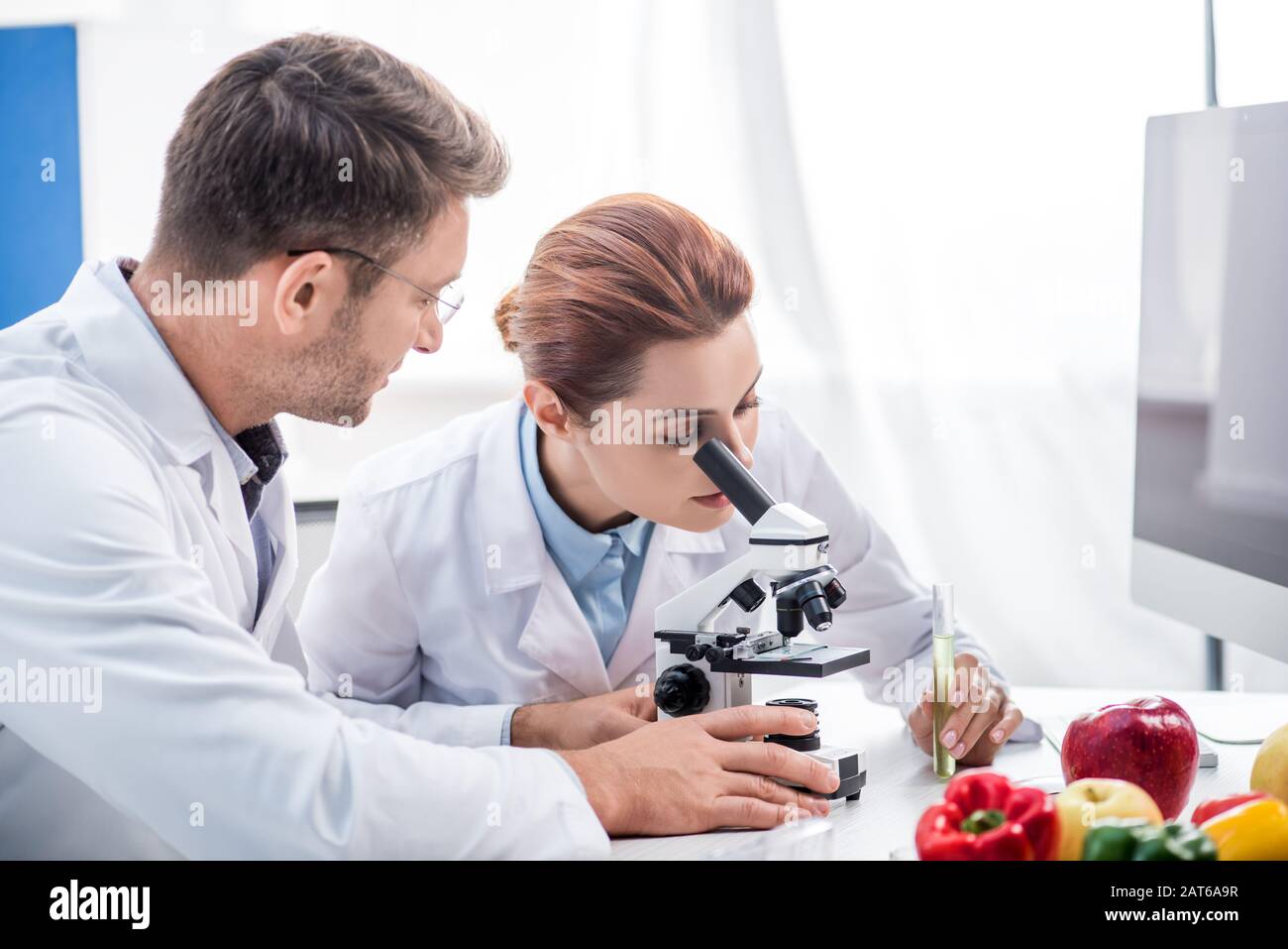 molecular nutritionist using microscope and colleague looking at her ...