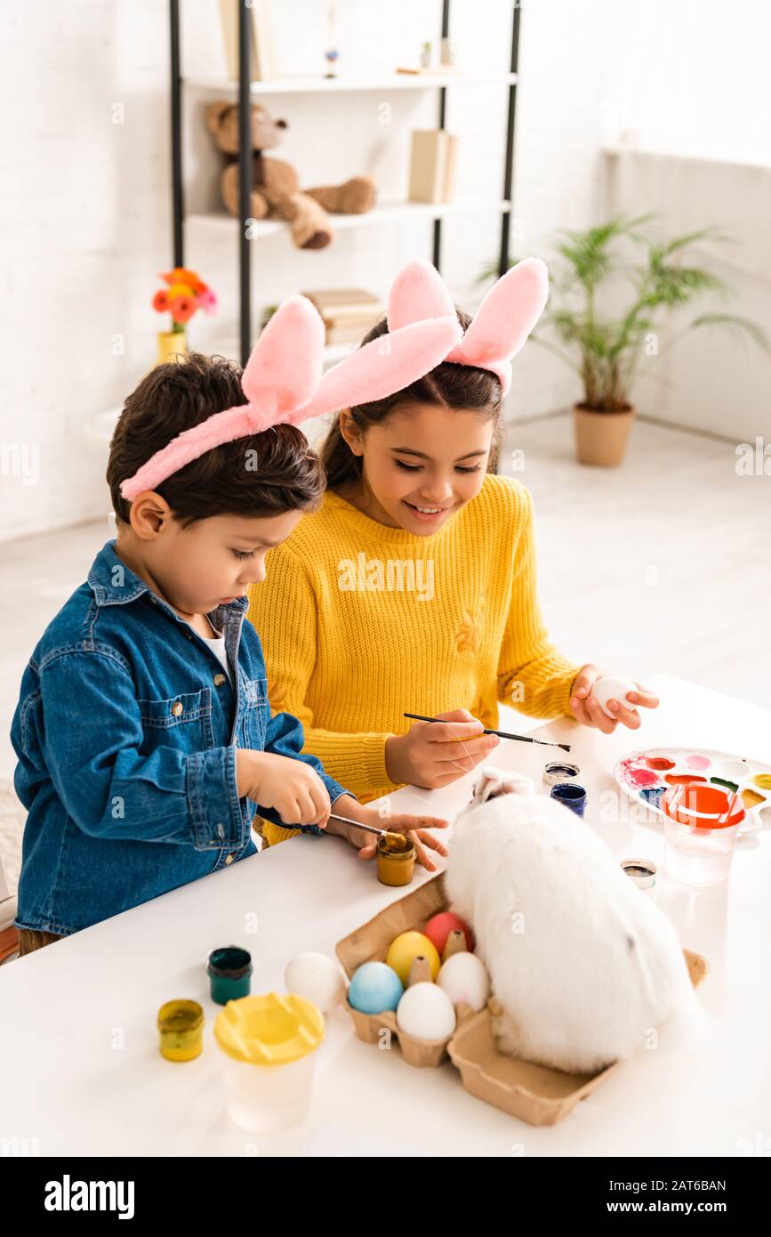 cute brother and sister in bunny ears painting Easter eggs while ...