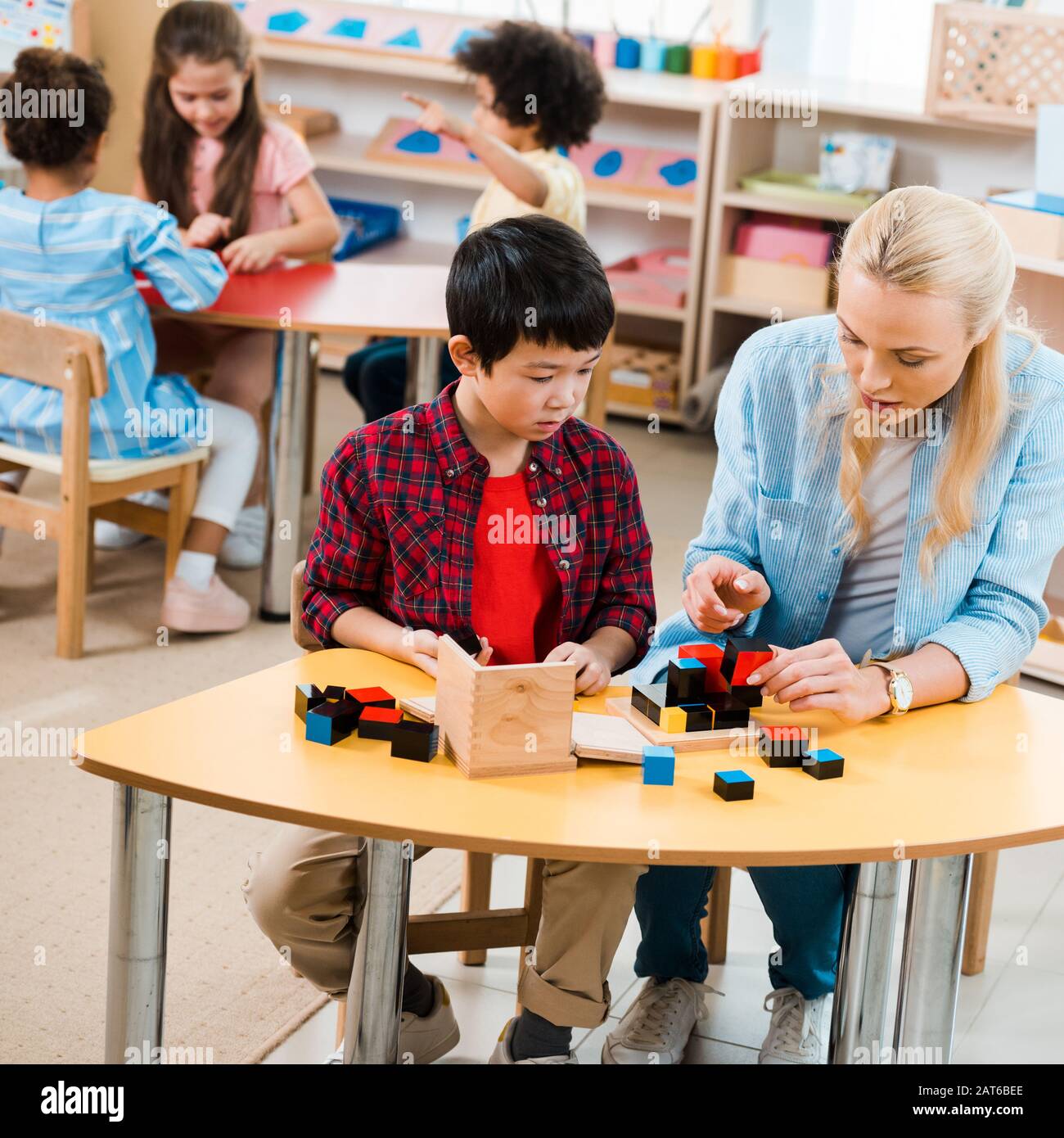 Selective focus of teacher and kid playing building blocks with ...