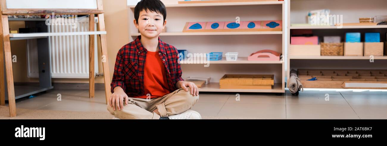 Panoramic shot of smiling asian kid sitting on floor in montessori ...