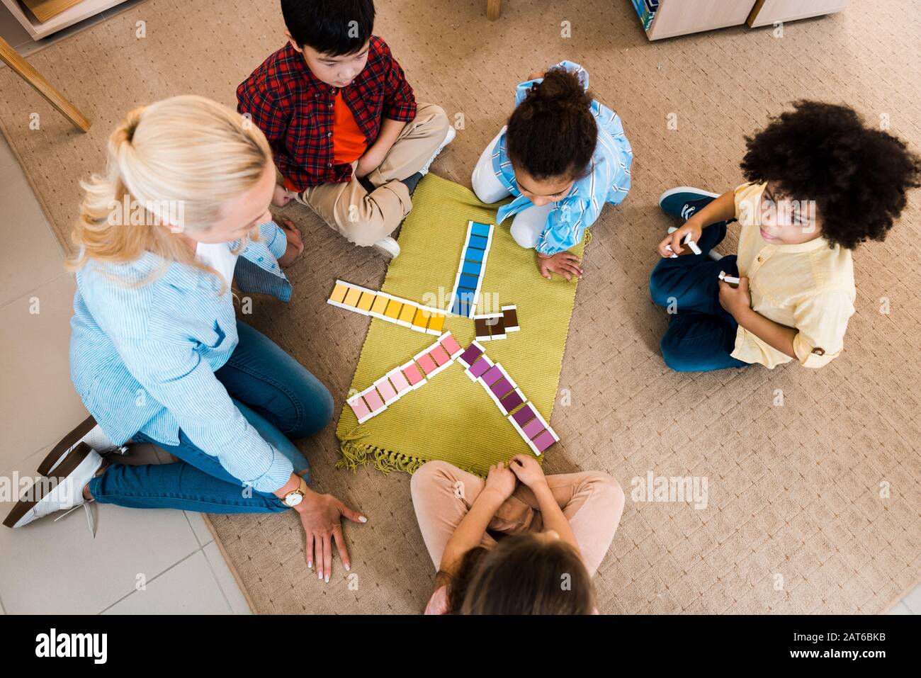Overhead view of teacher playing with kids educational game on floor in ...