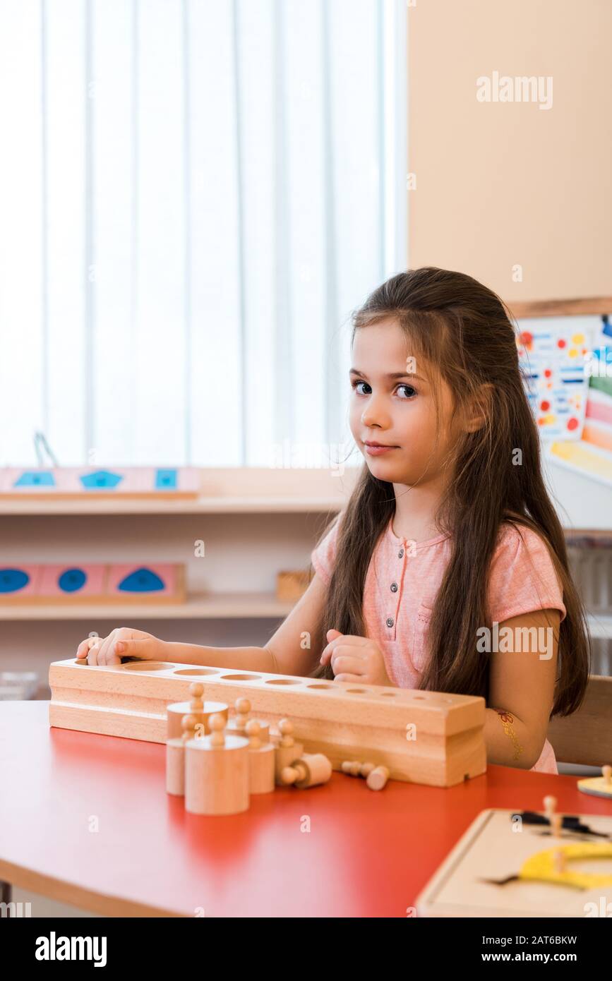 Kid folding educational game and looking at camera in montessori school ...