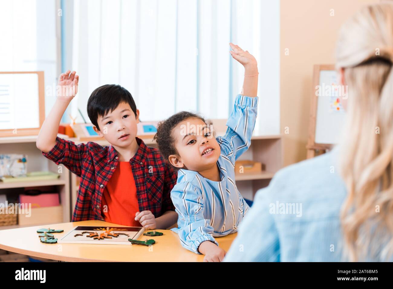 Selective focus of children with raised hands and teacher during lesson ...