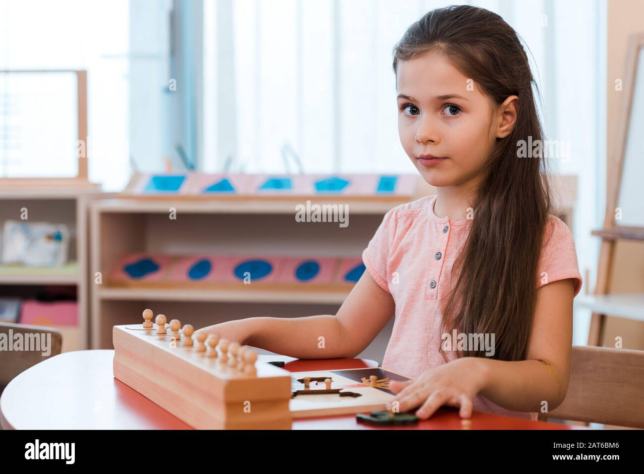 Child folding educational game and looking at camera at desk in ...