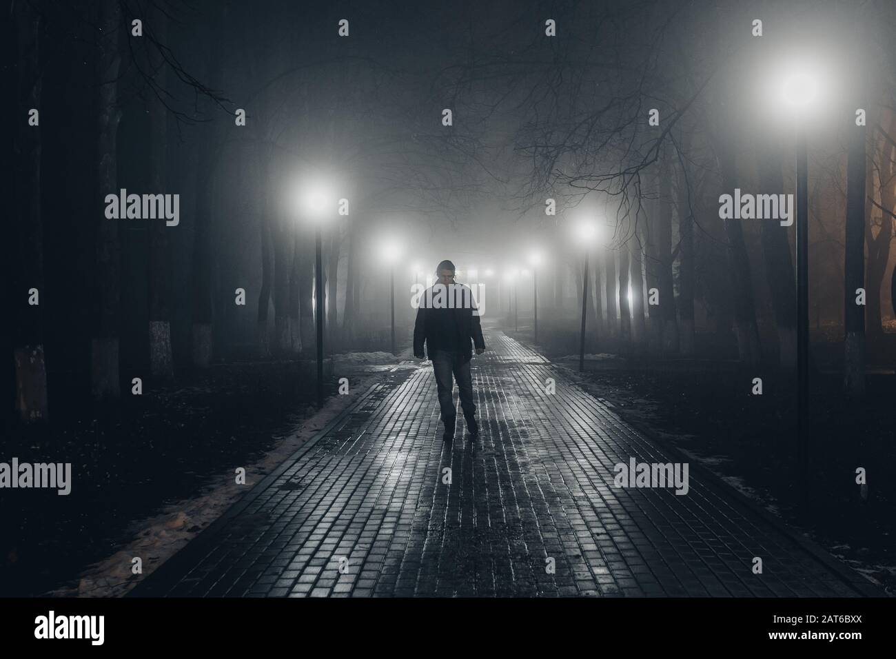 Sad man alone walking along the alley in night foggy park. front view ...