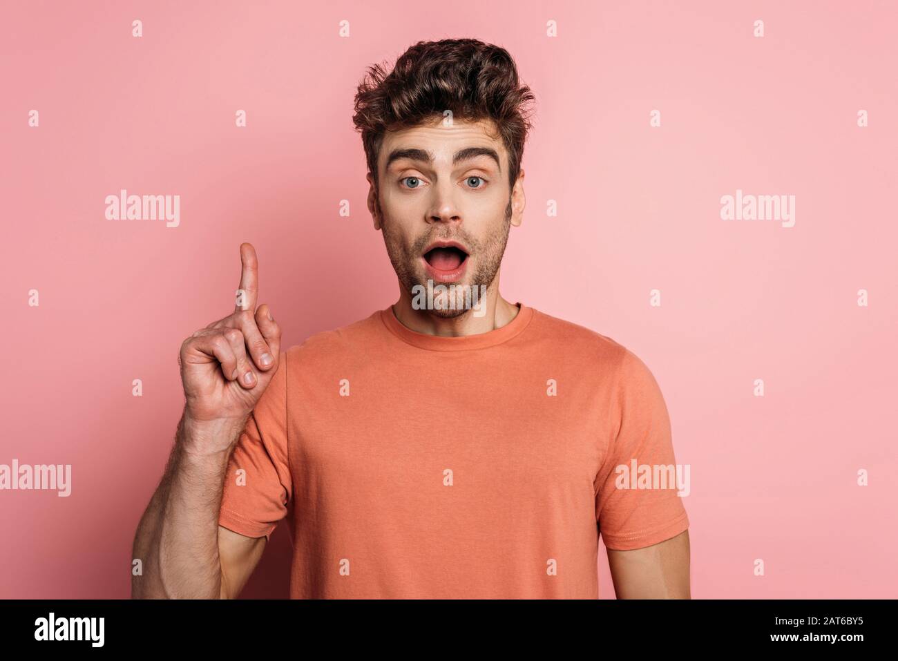 shocked man showing idea sign while looking at camera on pink ...