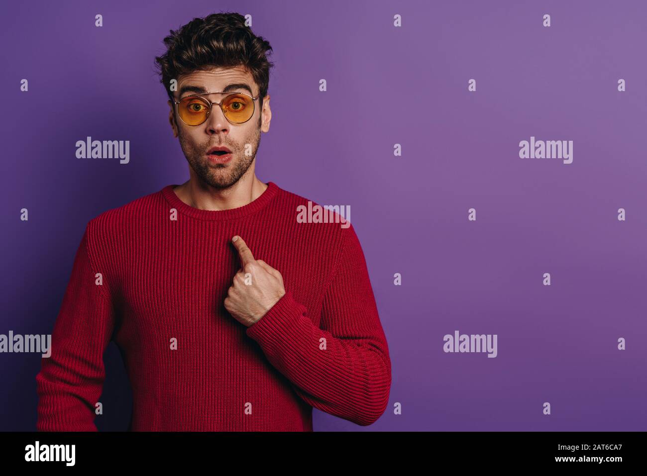 shocked young man pointing with finger at himself and looking at camera ...