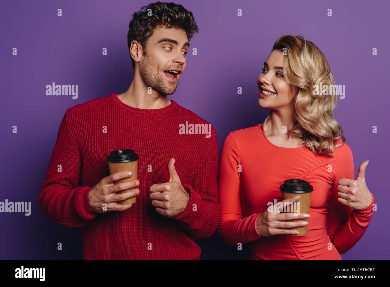 happy couple showing thumbs up while holding coffee to go on purple ...