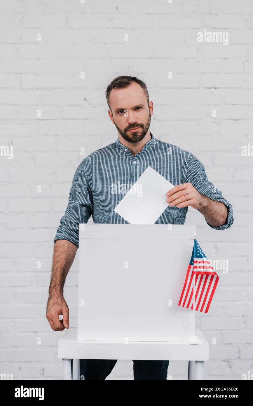 bearded and handsome voter putting blank ballot in voting box near ...