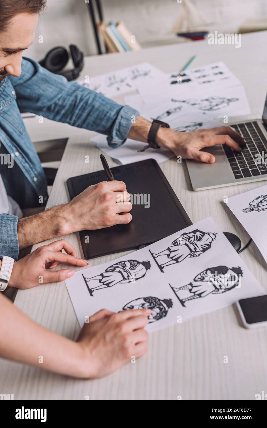 cropped view of animator pointing with finger at cartoon sketch near ...