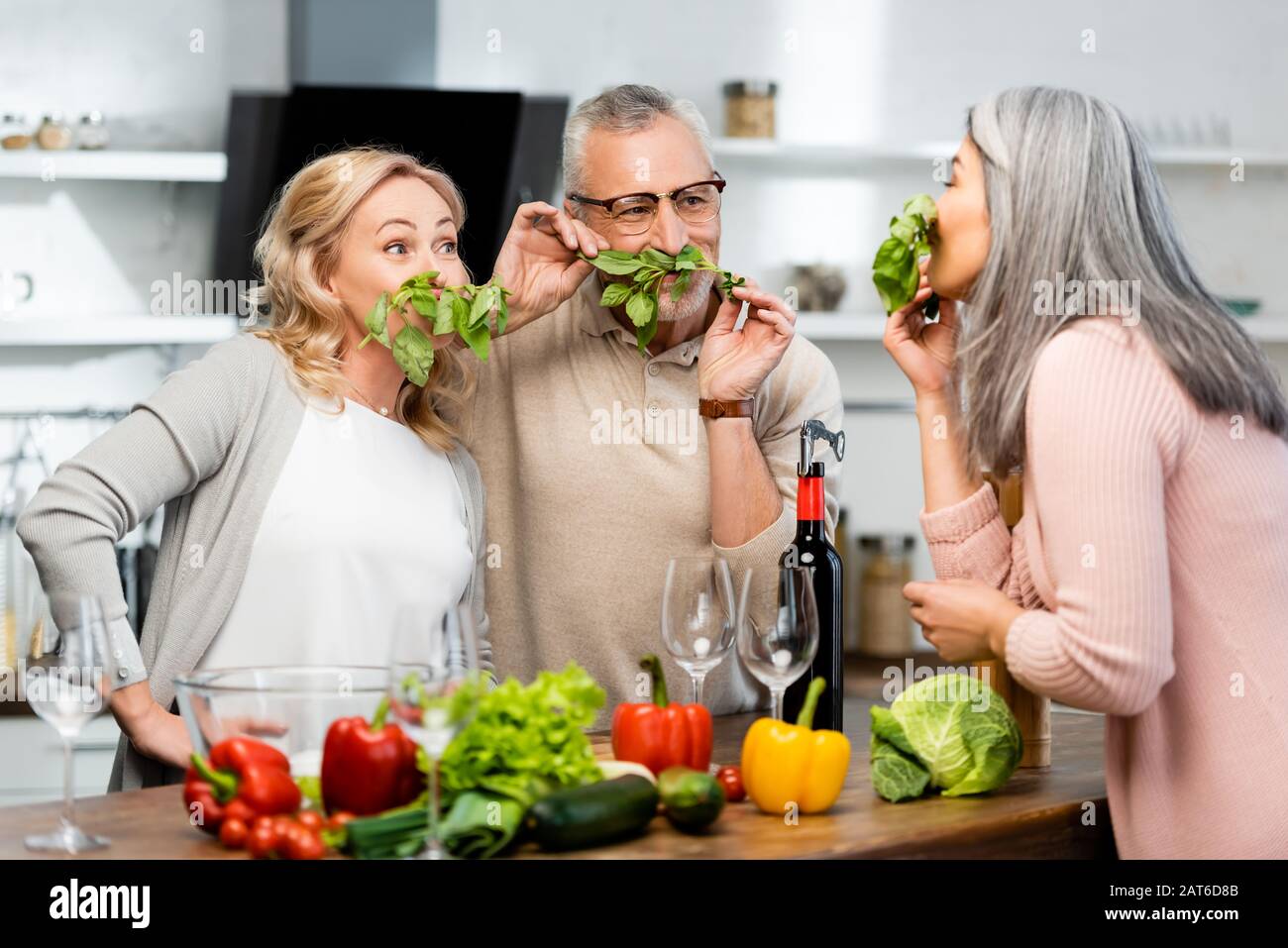 three smiling friends smelling organic and green basil in kitchen Stock ...