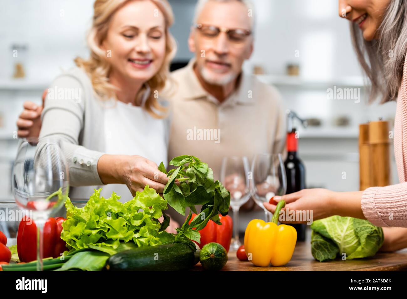 selective focus of smiling friends looking at basil in kitchen Stock ...
