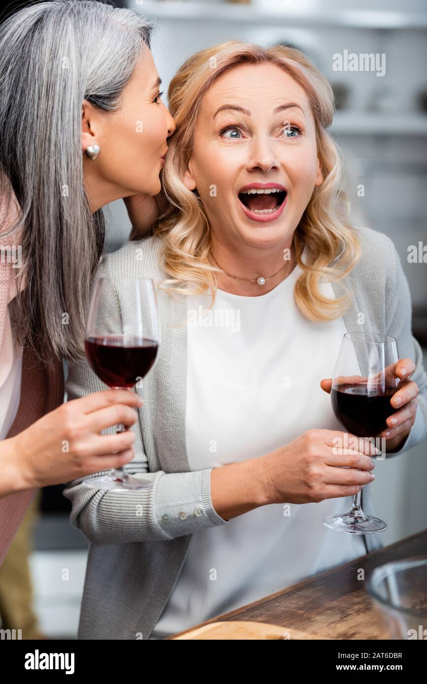 asian woman telling secret to shocked friend with wine glass Stock ...