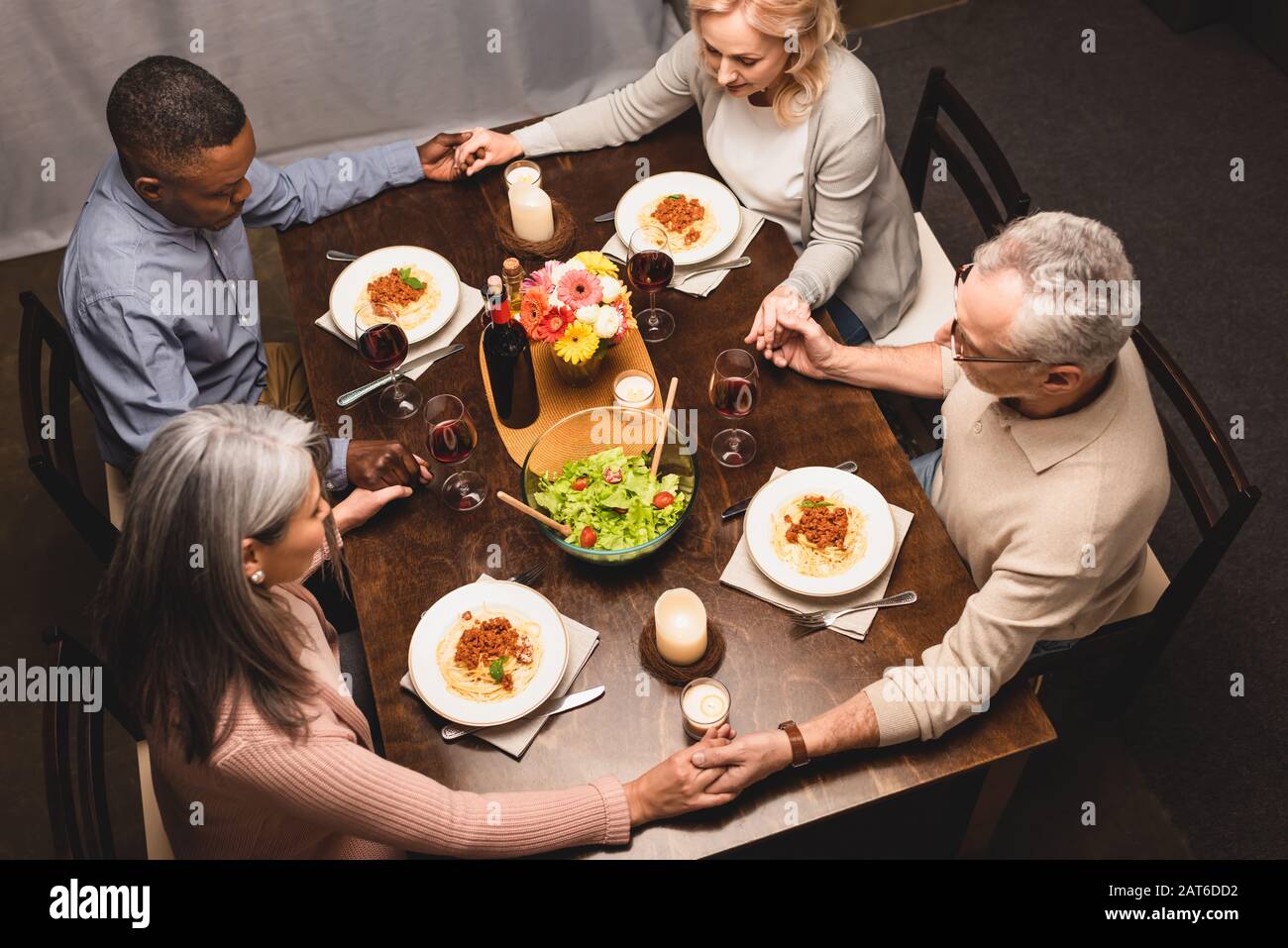 overhead view of multicultural friends holding hands and praying during ...