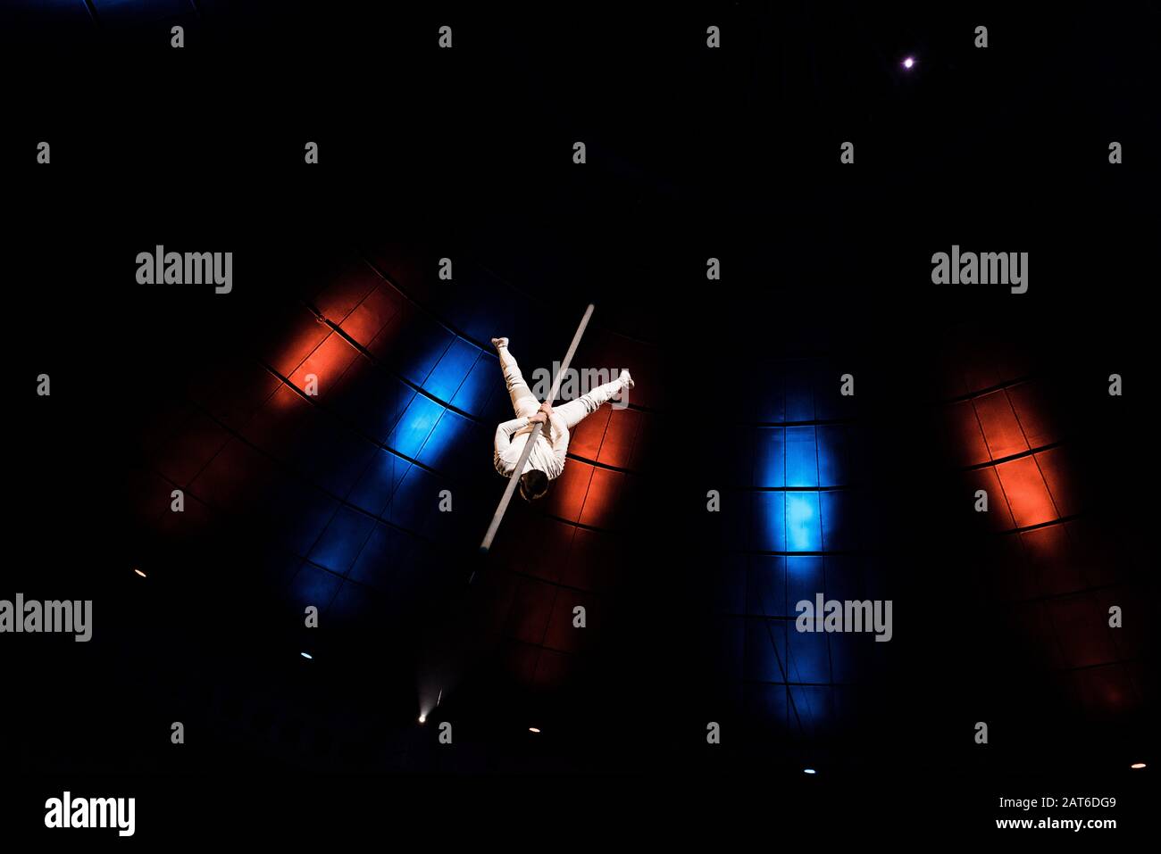 back view of acrobat balancing on metallic pole in arena of circus ...