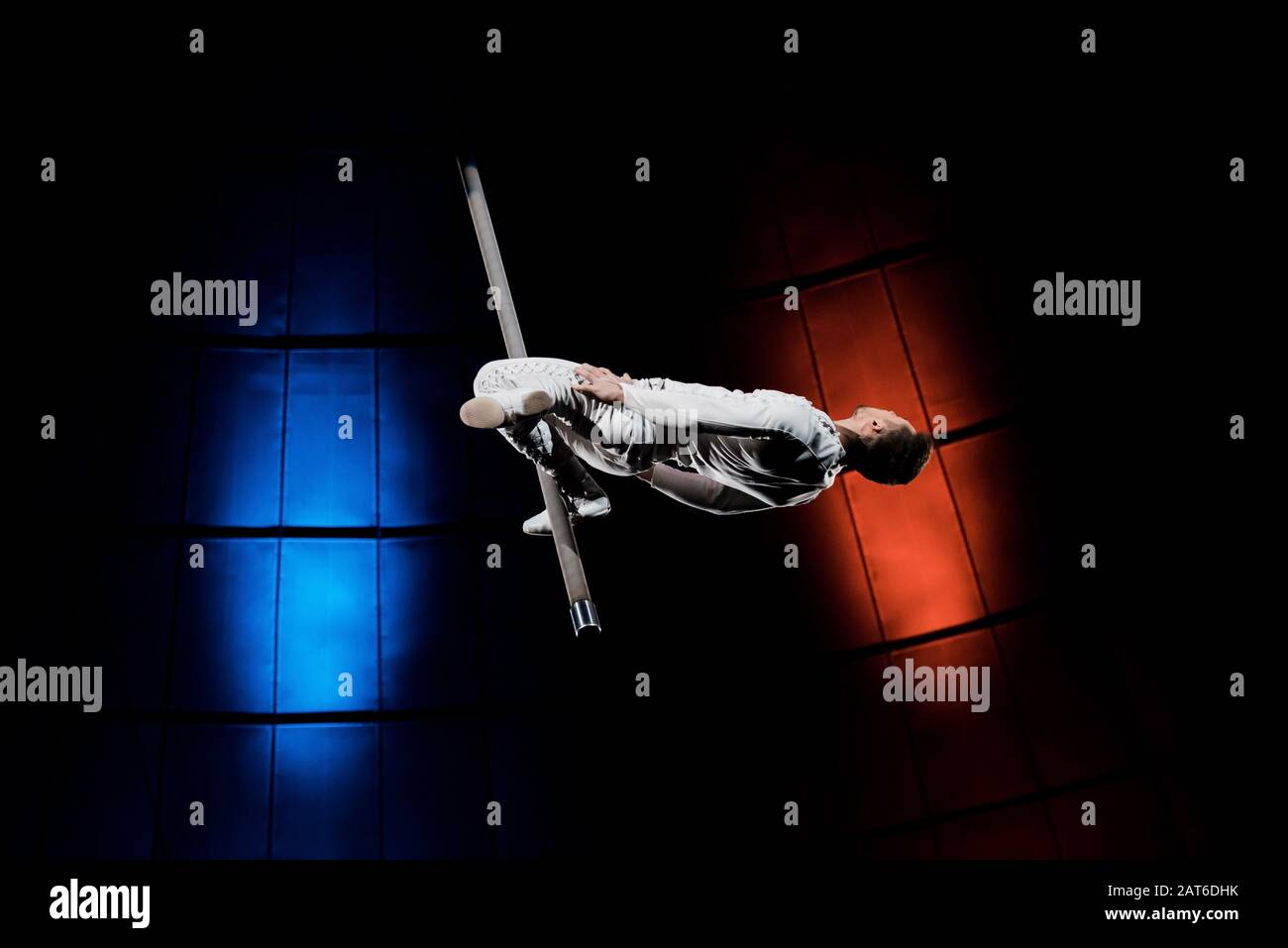 athletic acrobat balancing on metallic pole near blue and red lighting ...