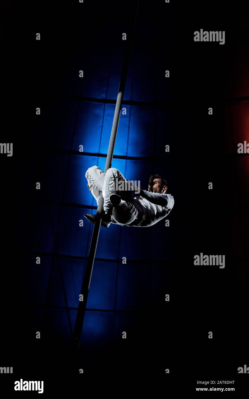 handsome and strong acrobat performing on metallic pole neat blue light ...
