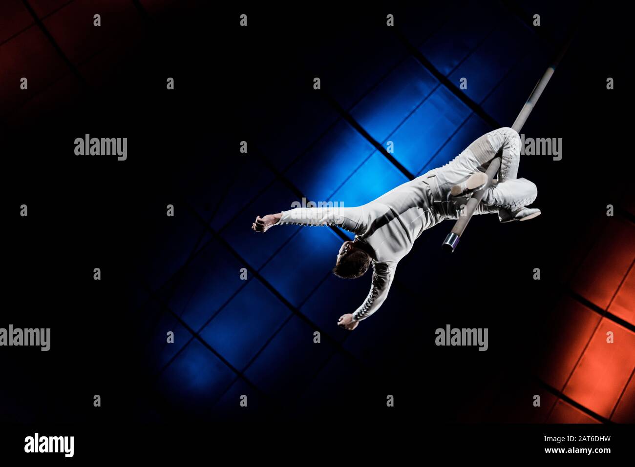 back view of strong acrobat balancing on metallic pole near blue and ...