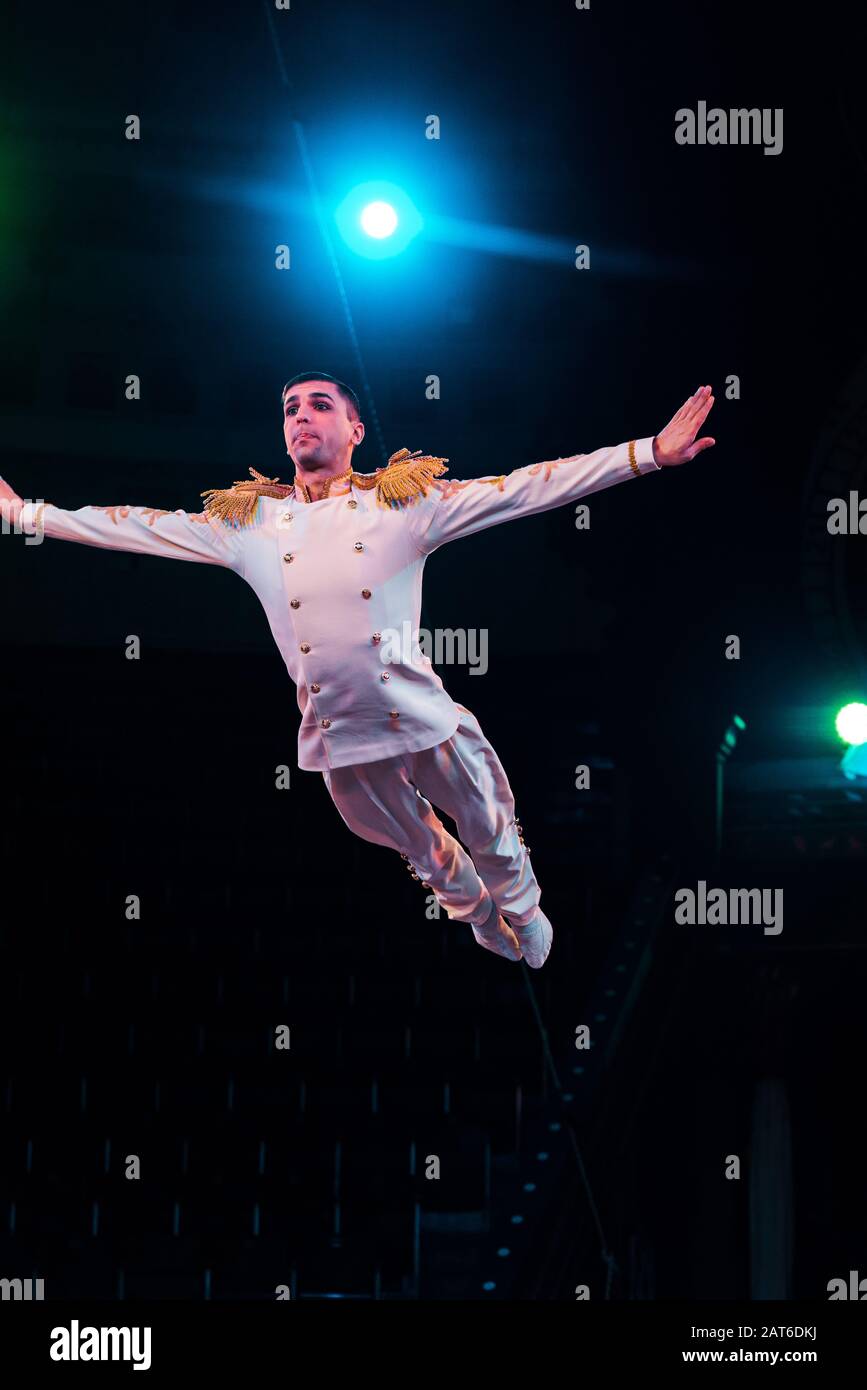 handsome air acrobat with outstretched hands flying in arena of circus ...