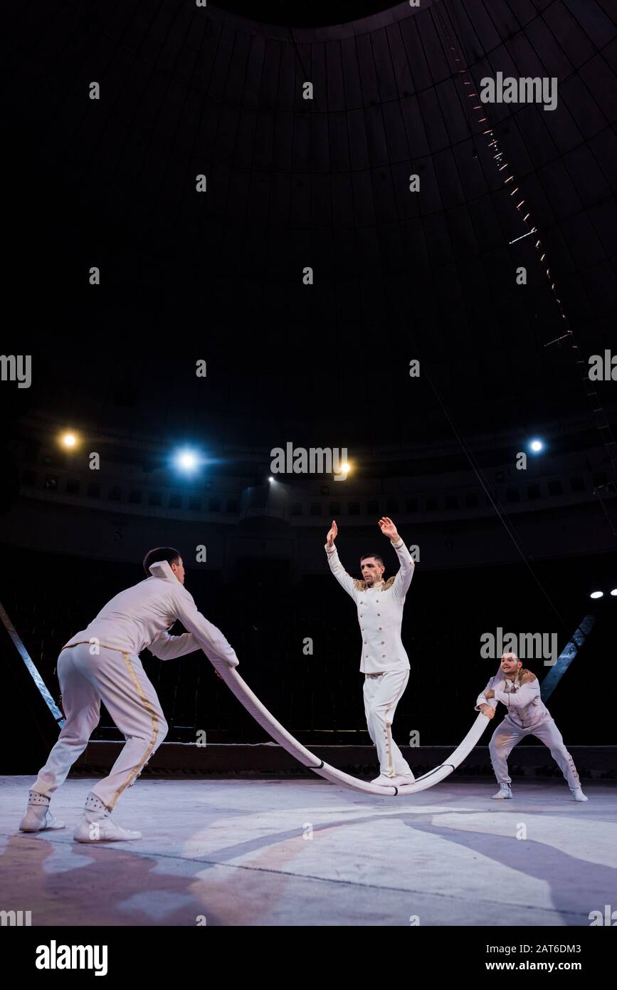acrobats supporting man with outstretched hands ready to jump on pole ...