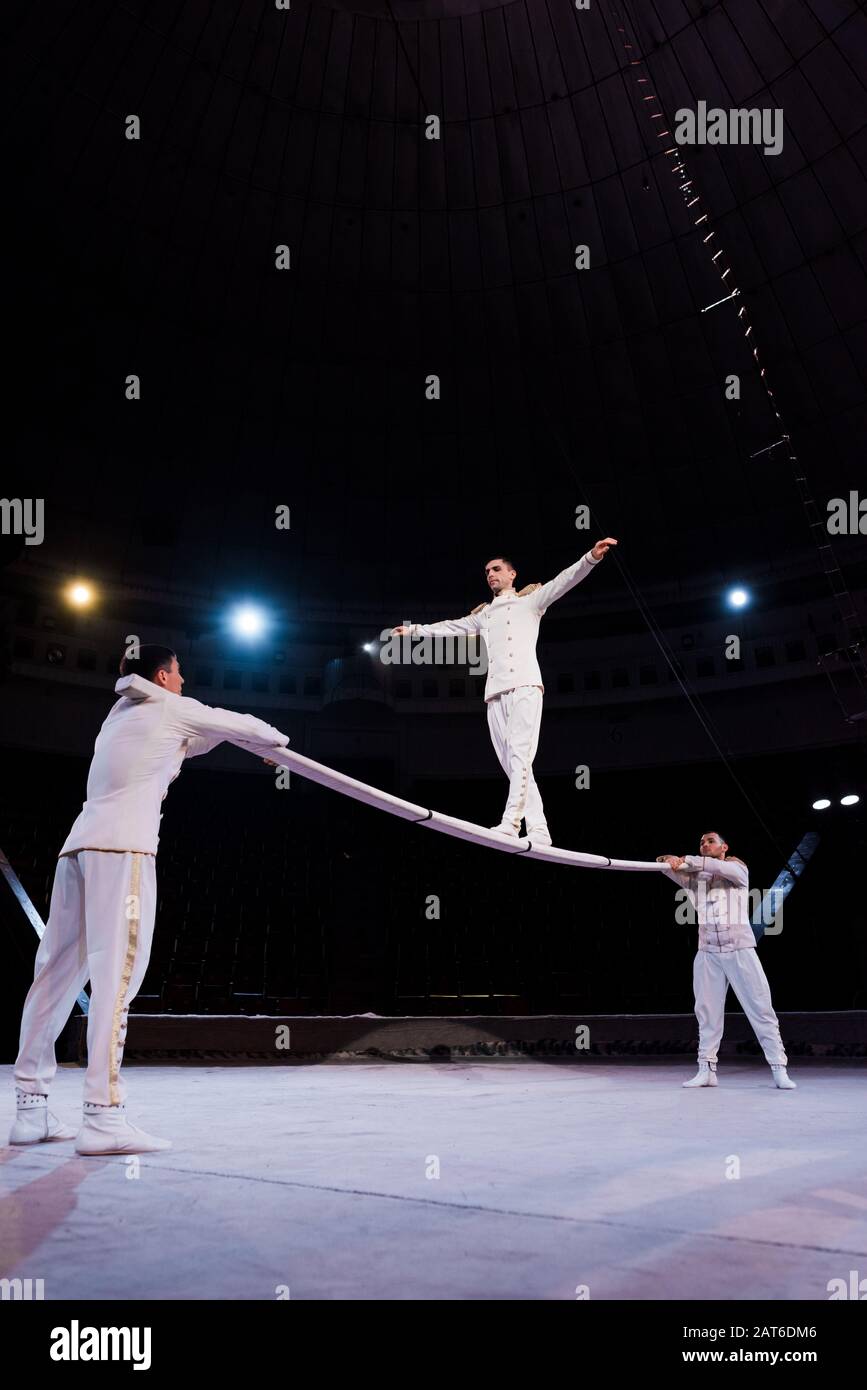 acrobats supporting man with outstretched hands walking on metallic ...