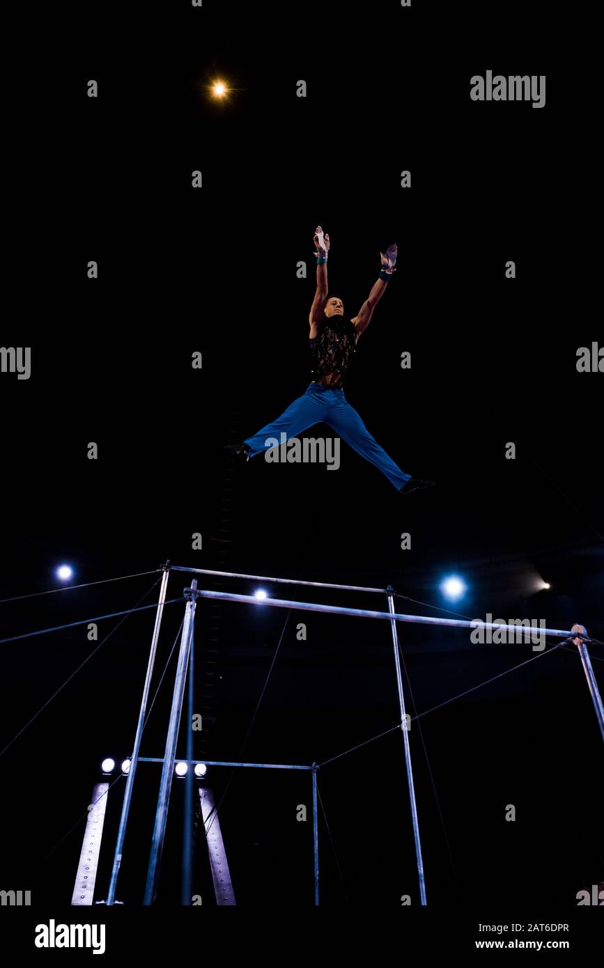 low angle view of gymnast jumping near horizontal bars in arena of ...