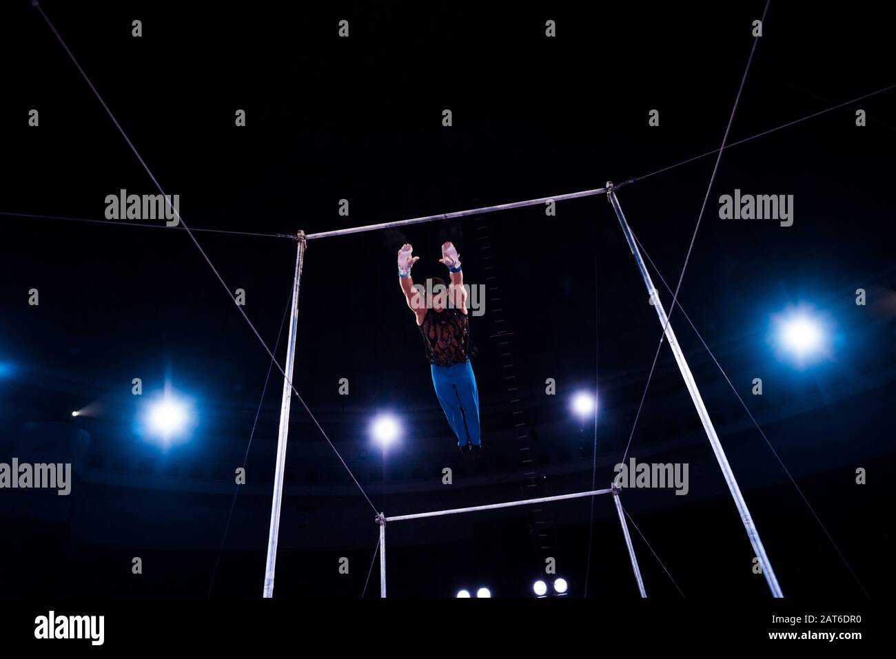 athletic gymnast jumping while performing on horizontal bars in arena ...