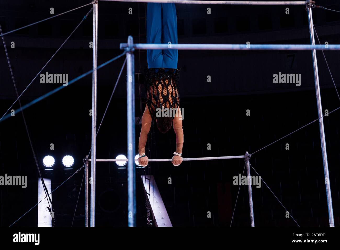 back view of athletic gymnast performing on horizontal bars in arena of ...