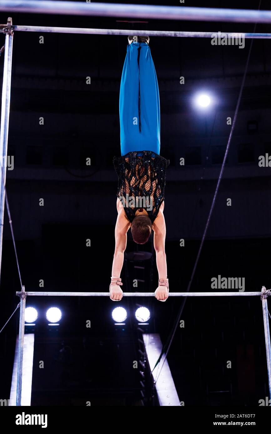 back view of strong gymnast performing on horizontal bars in arena of ...