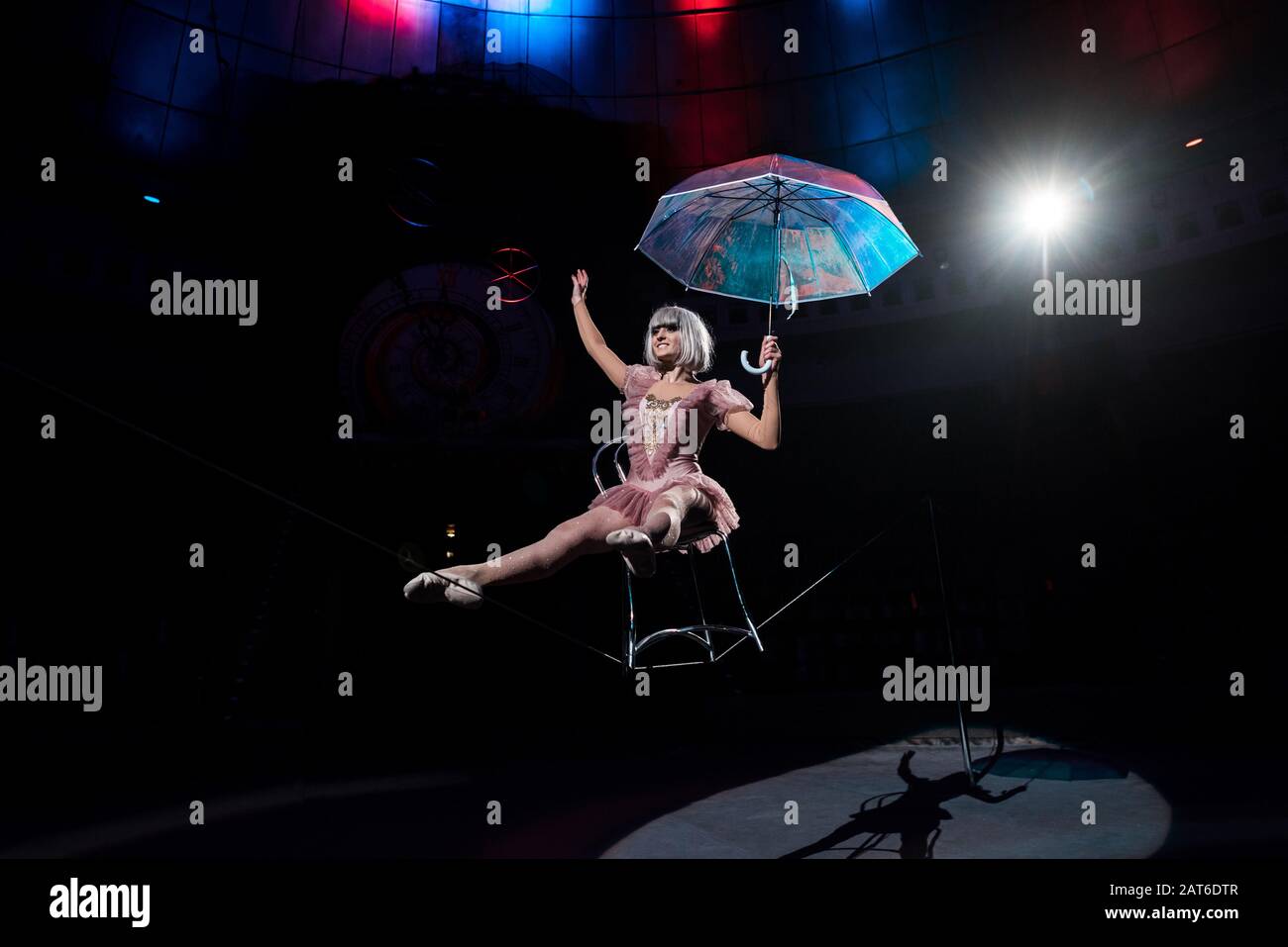 aerial acrobat holding umbrella and balancing on rope while sitting on ...