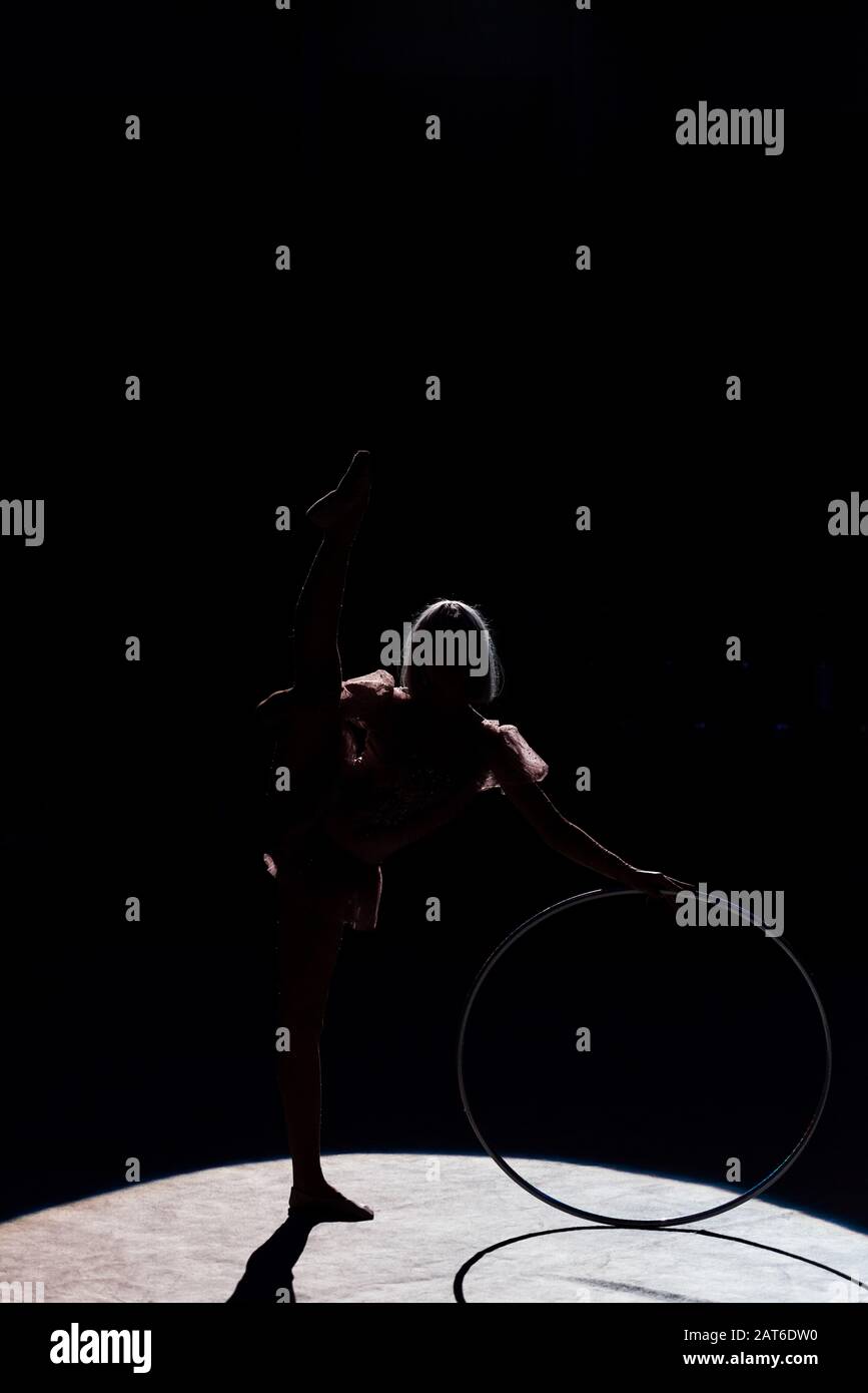 silhouette of flexible acrobat standing with hula hoop in arena of ...