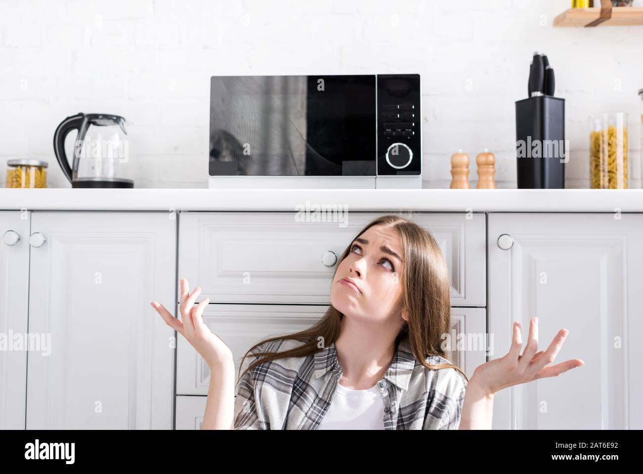 confused and attractive woman looking at microwave and doing shrug ...
