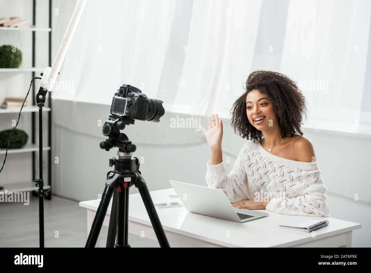 happy african american influencer in braces waving hand near digital ...
